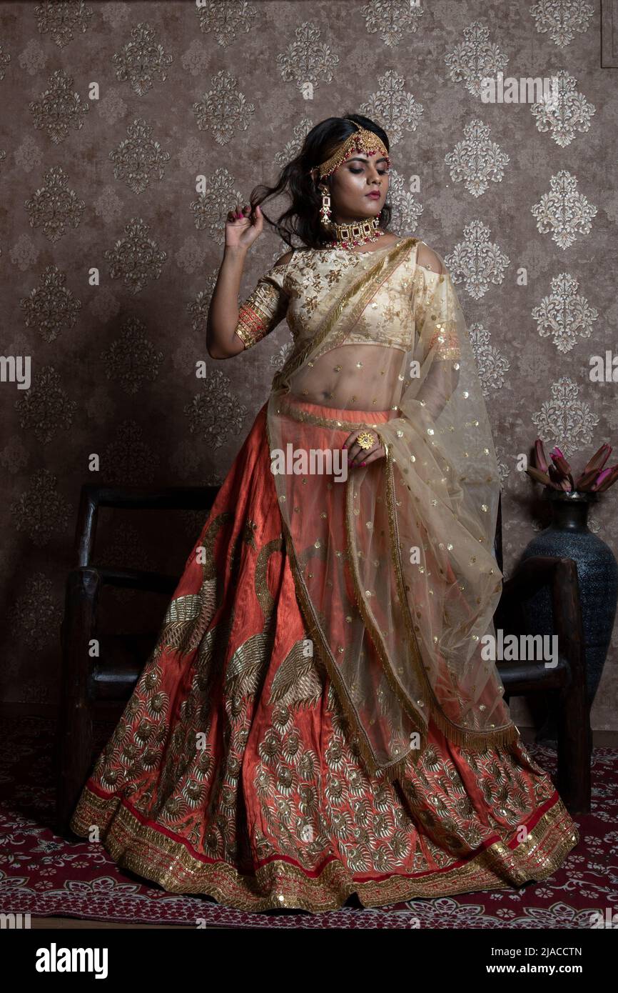 Indian female model wearing an orange and beige lehemga and jewellry ...