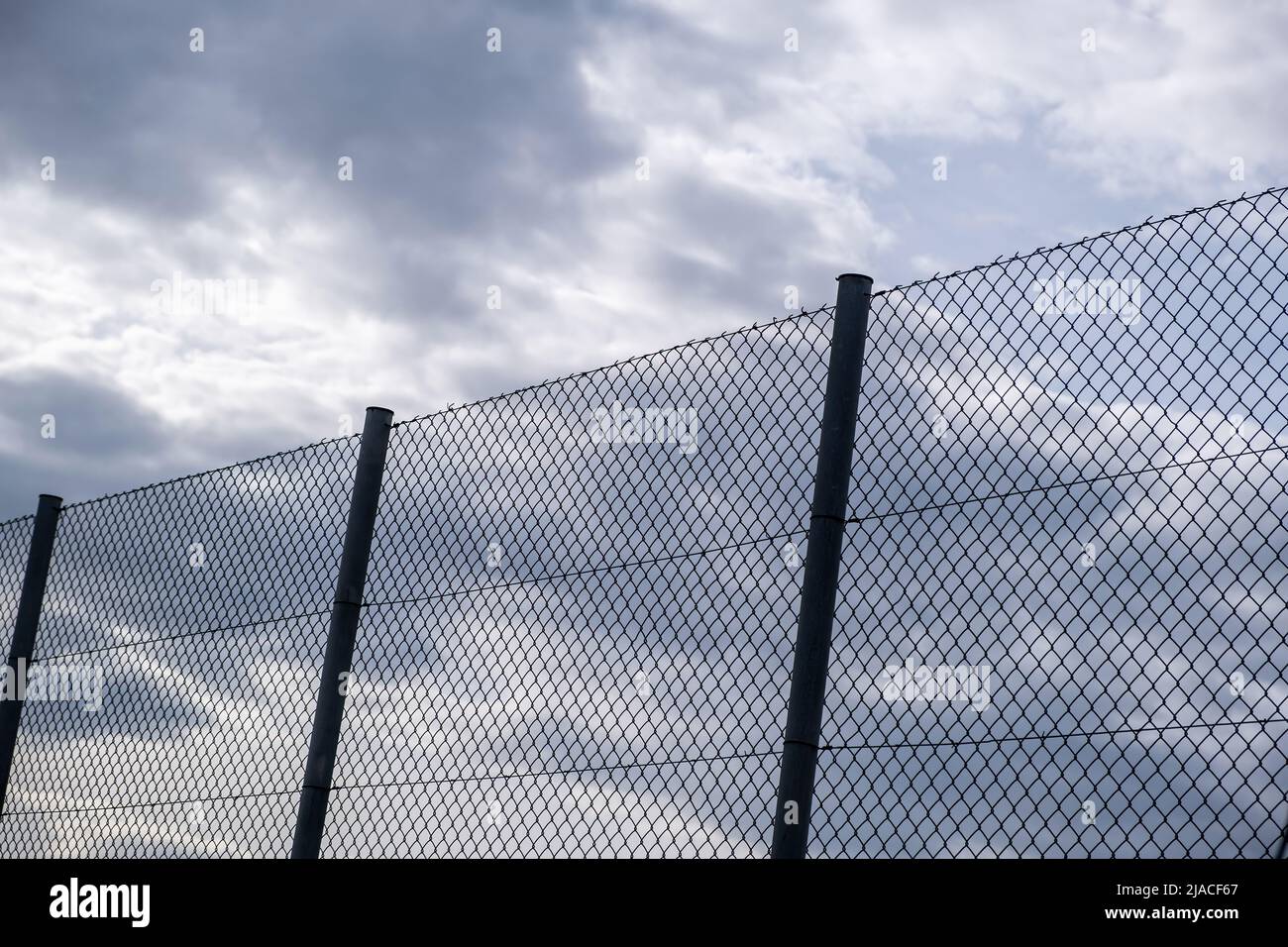 Wire mesh fence on cloudy sky background, low angle view. Metallic ...
