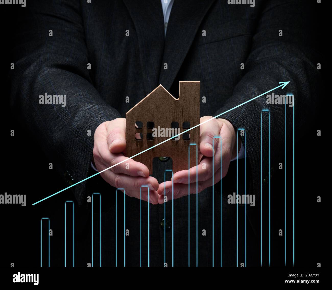 Hand holds a wooden model of a house on a dark background. Real estate ...