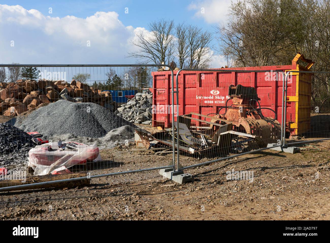 Red builder skip and construction materials behind steel security ...
