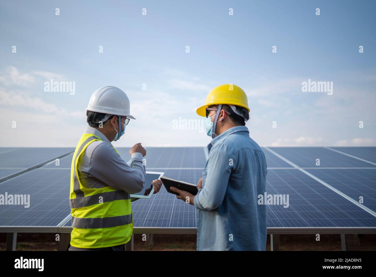 Two engineers standing next to solar panels at a solar powered station ...