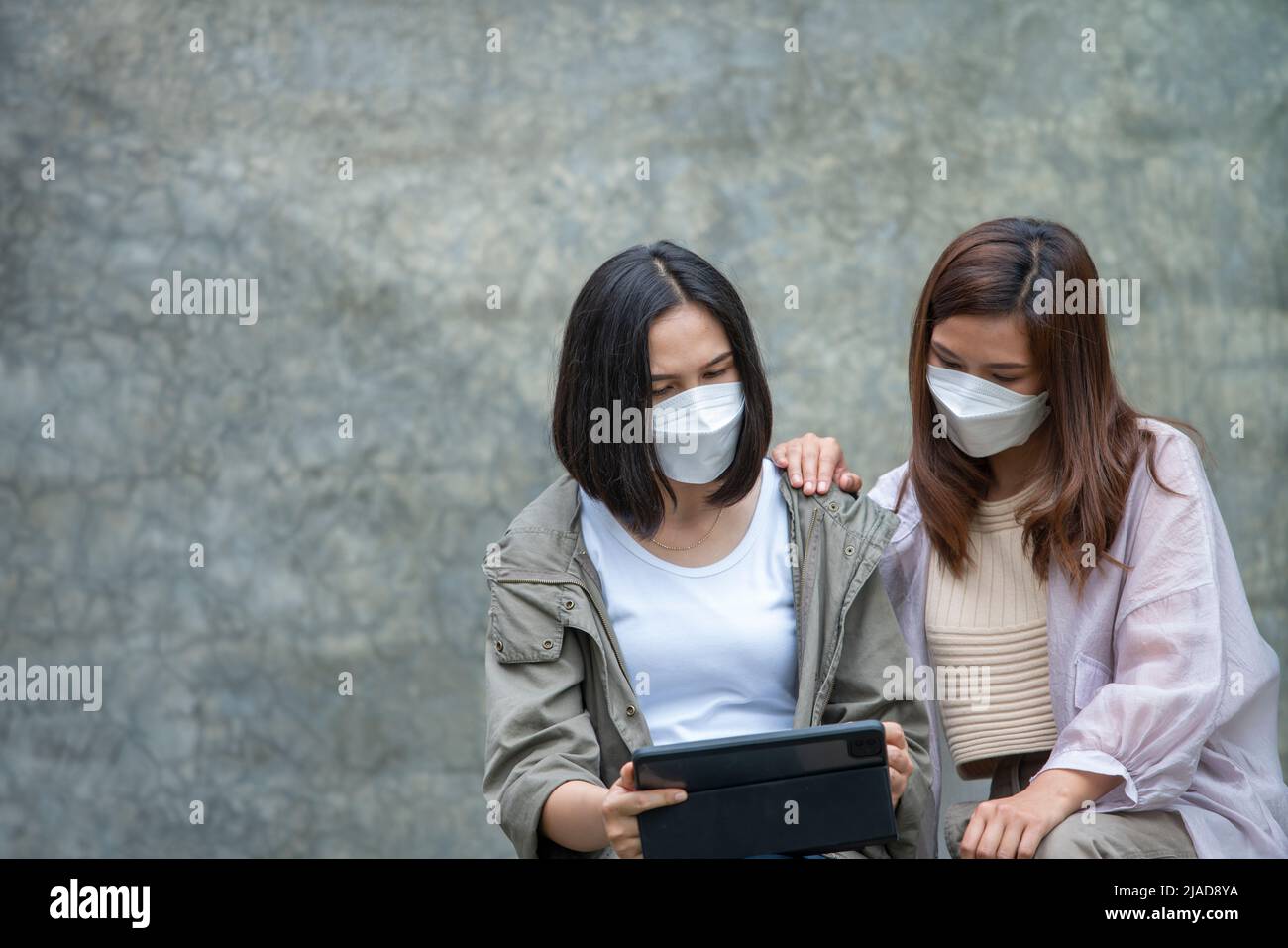 Two woman wearing face masks sitting side by side looking at a digital ...
