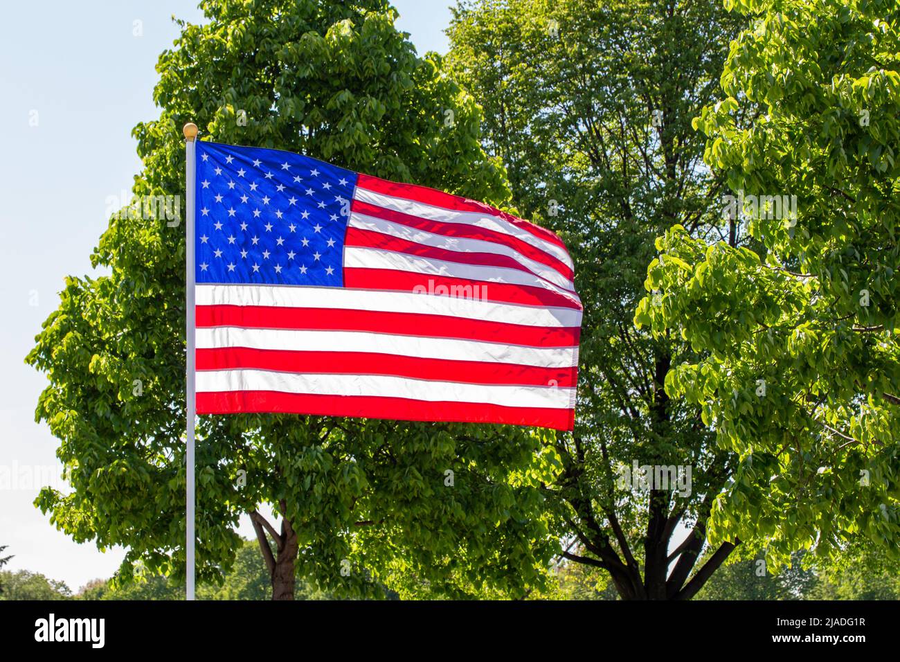 Close up view of an outdoor American flag in a light breeze, with trees ...