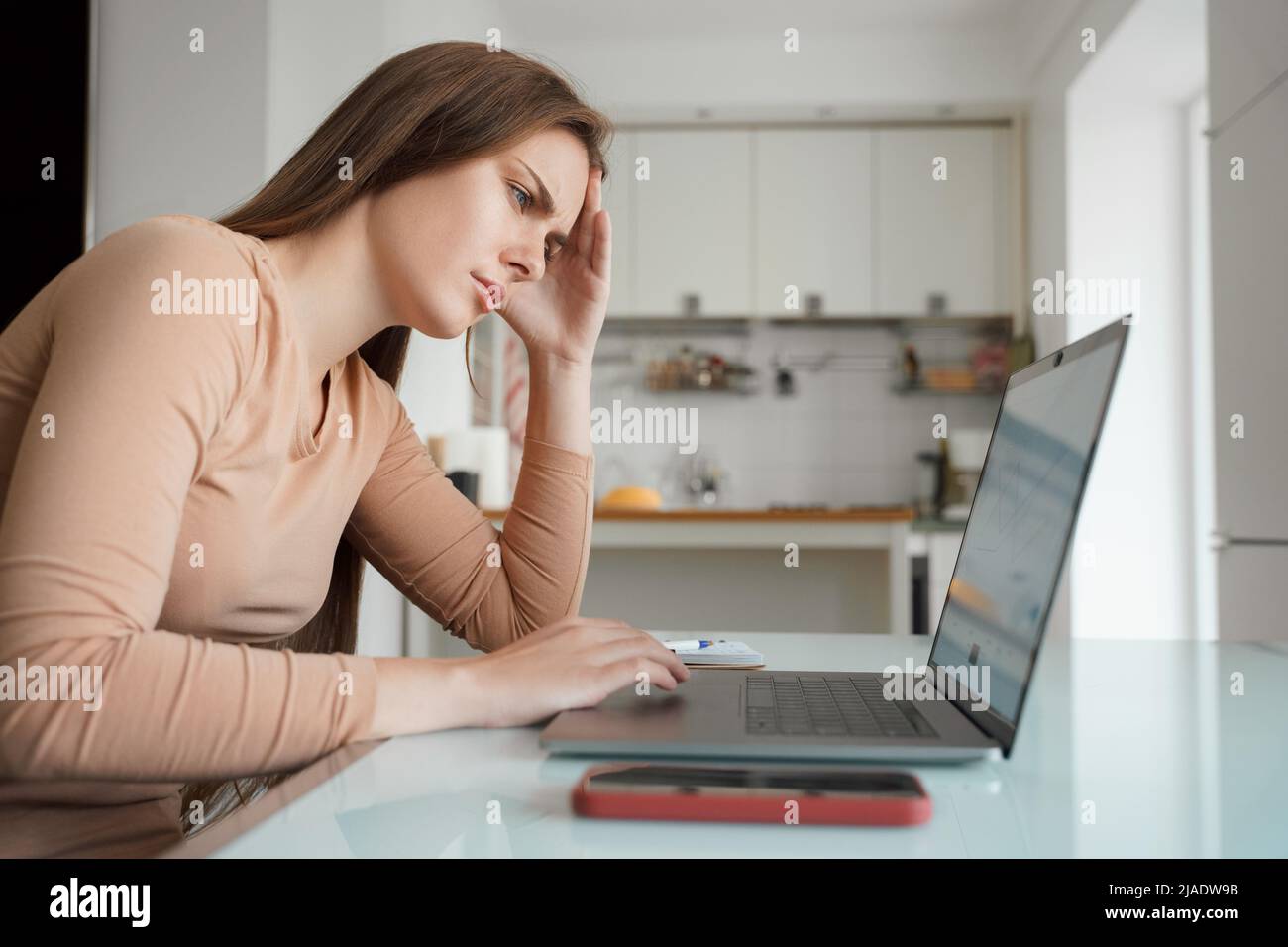 Side view sad woman looking at laptop screen with leaned head on hand ...