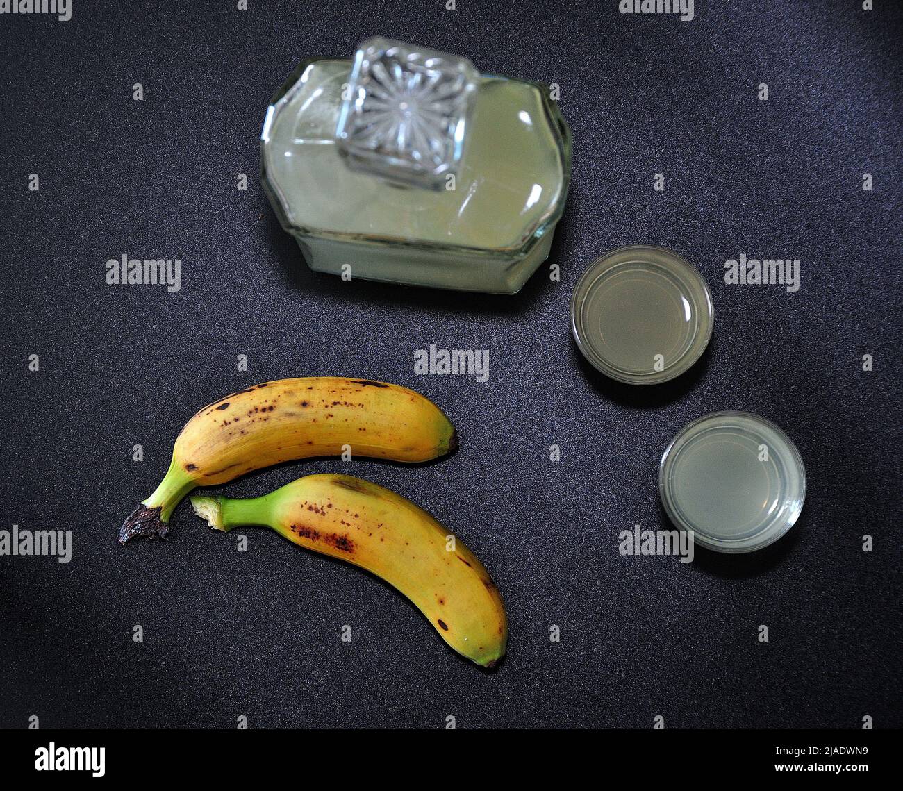 Banana liqueur, strong homemade alcohol and ripe fruits on a black ...