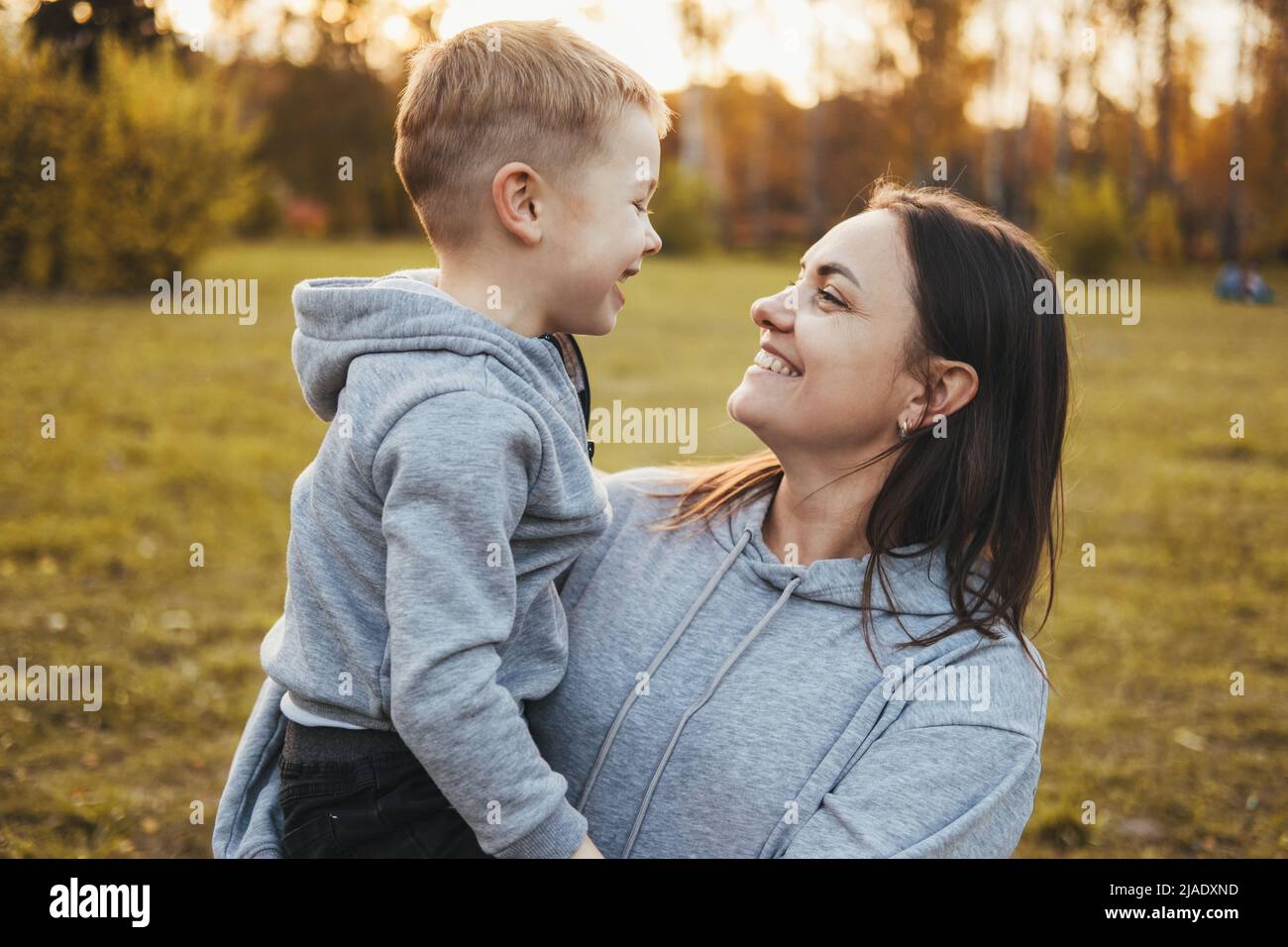 Little boy holded by his mom in the arms which is laughing. Side view ...