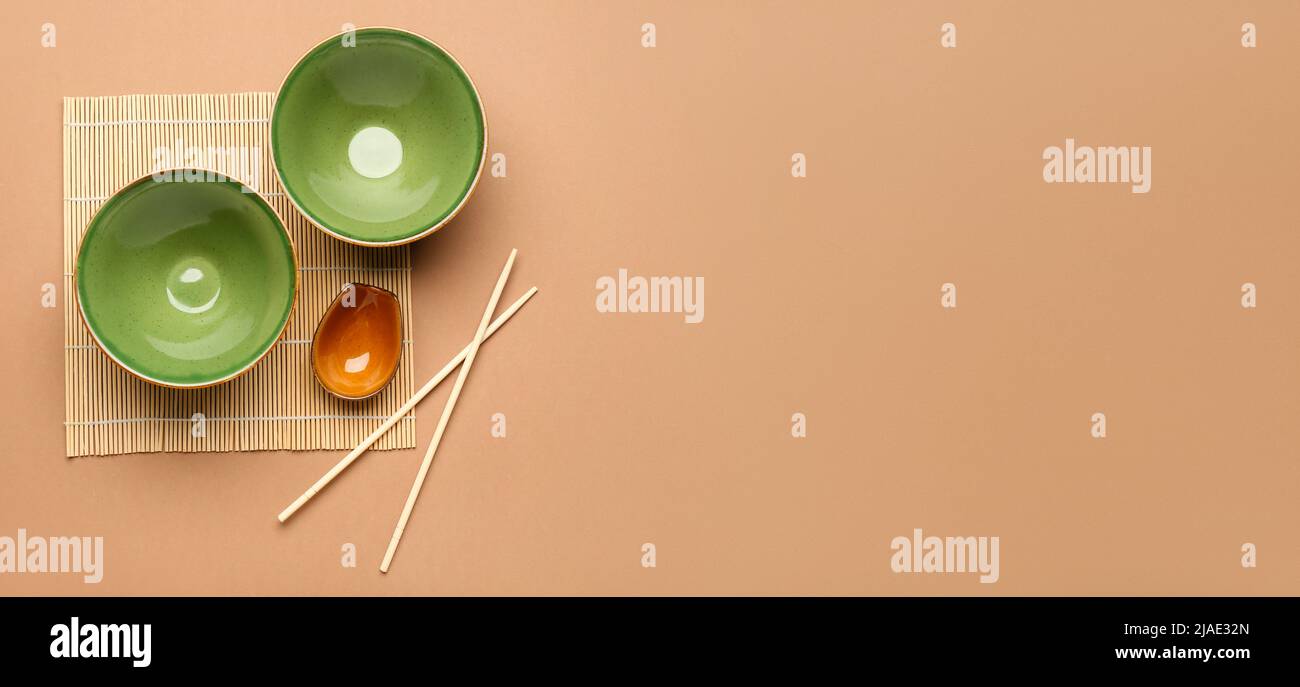 Chinese bowls with chopsticks and bamboo mat on color background with ...