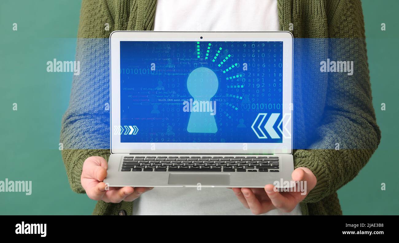 Young man holding laptop with blocked screen on green background ...