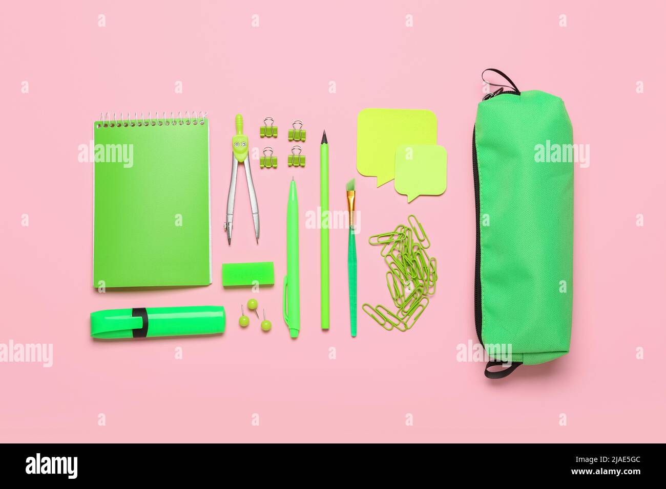Green pencil case with paper clips and school stationery on pink ...
