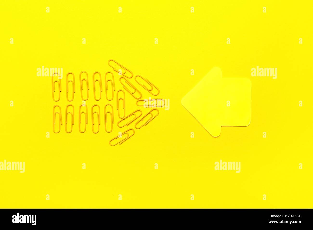 Arrow made of paper clips and sticky note on yellow background Stock ...