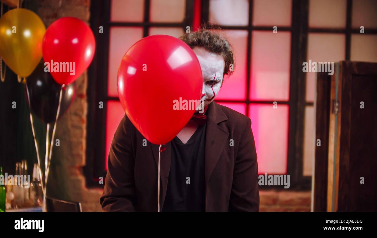 A scary clown peeking out from the red balloon Stock Photo - Alamy