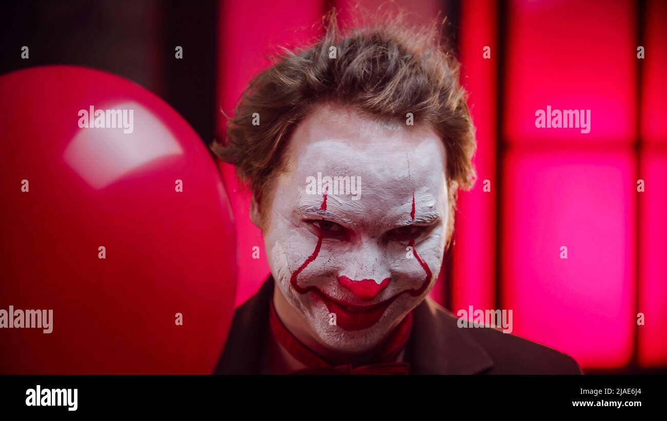 A scary clown holding a red balloon and creepy smiling Stock Photo - Alamy