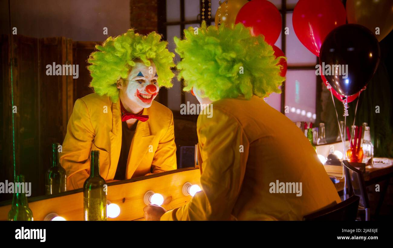 A crazy man clown in full costume looking in the mirror and smiling ...