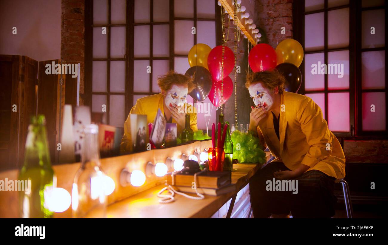 A sad man clown sitting in front of the mirror and smoking a cigarette ...