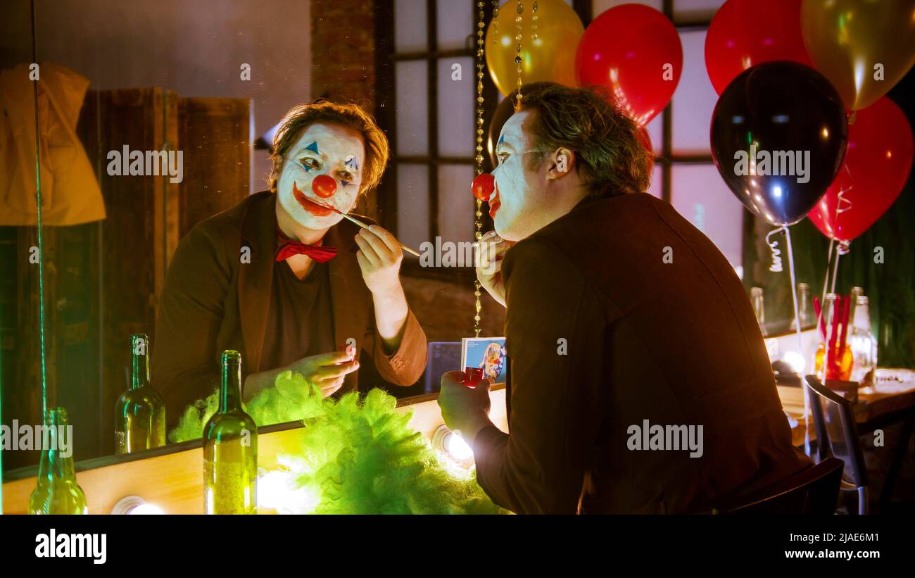 A man applying clown paint in his face in front of the mirror in the ...