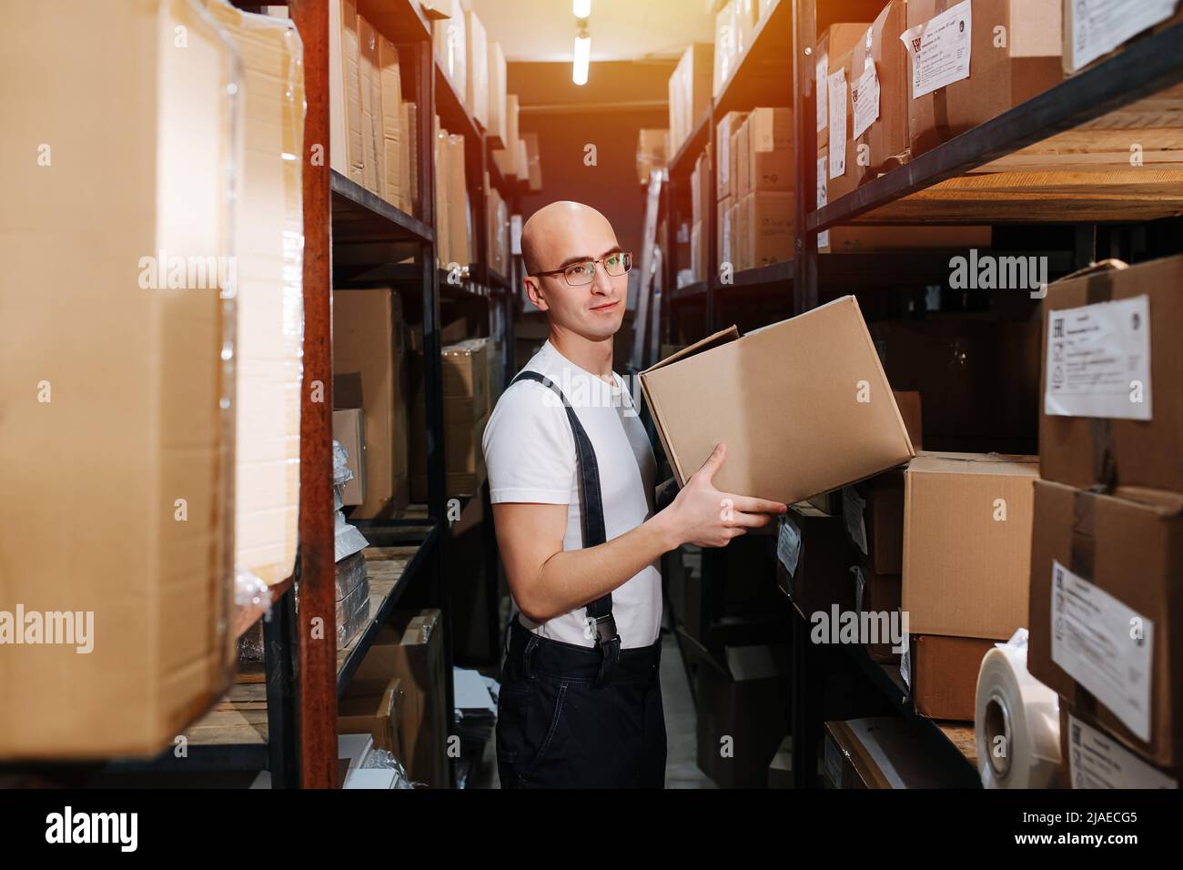Thougtful male warehouse worker holding a box, spacing out. He is ...