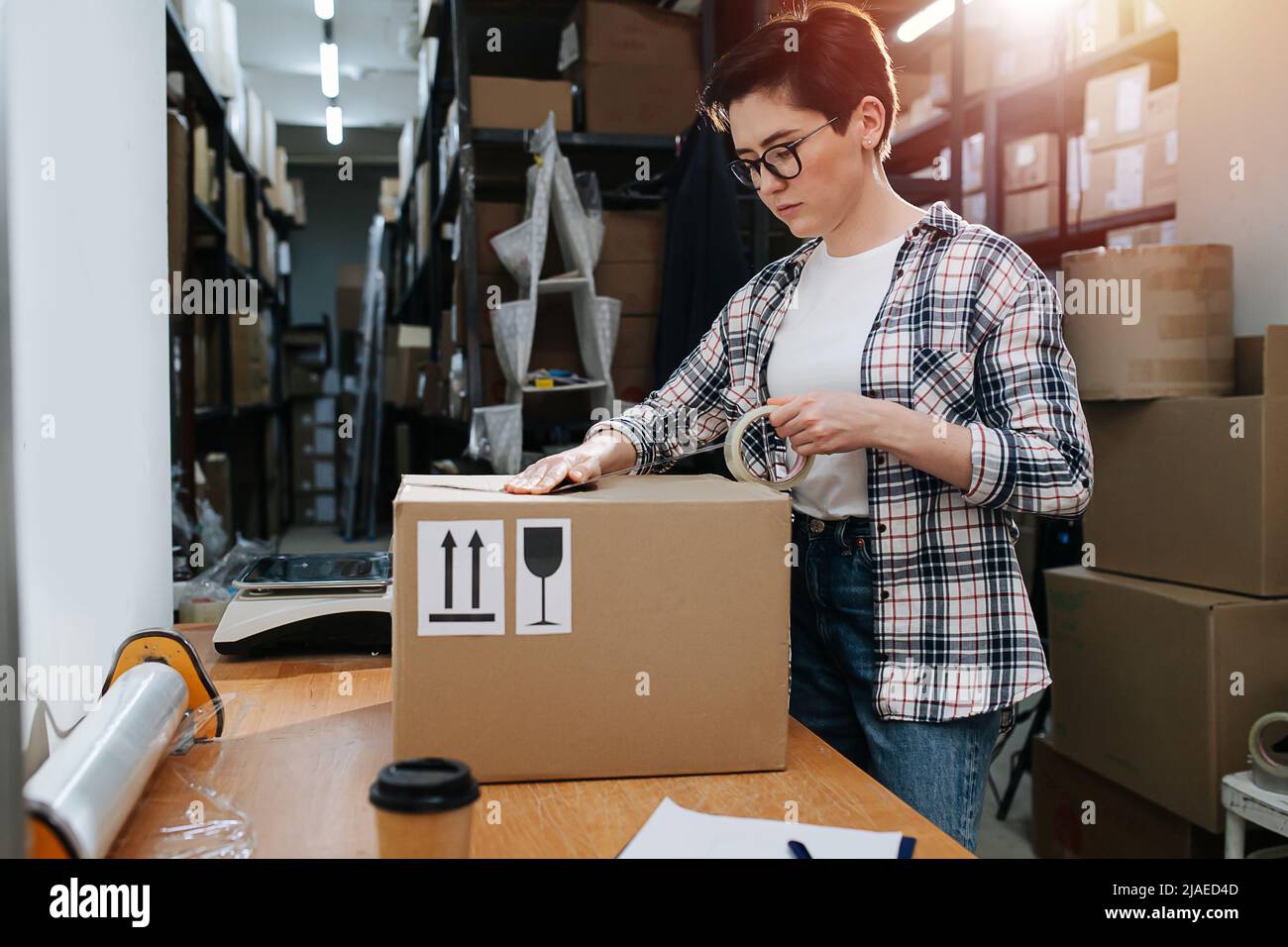 Focused short haired female warehouse worker packing a cardboard box ...