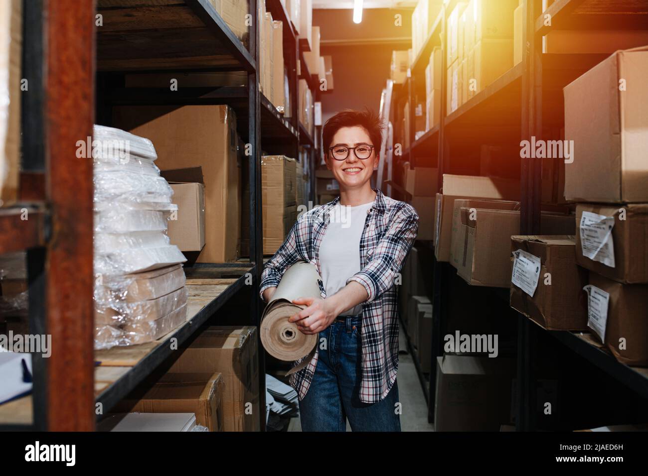 Proud happy female warehouse worker holding a big paper roll, standing ...