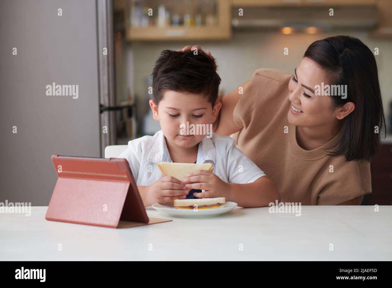 Happy mother shuffling hair of little son eating sandwiches for breakfast Stock Photo - Alamy