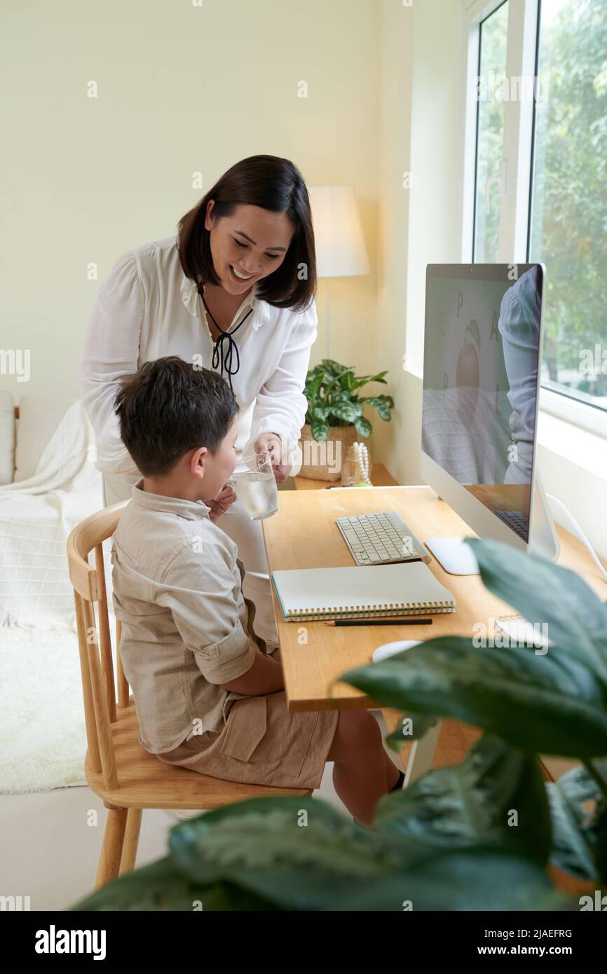 Smiling mother giving son glass of water when he is como learning ...