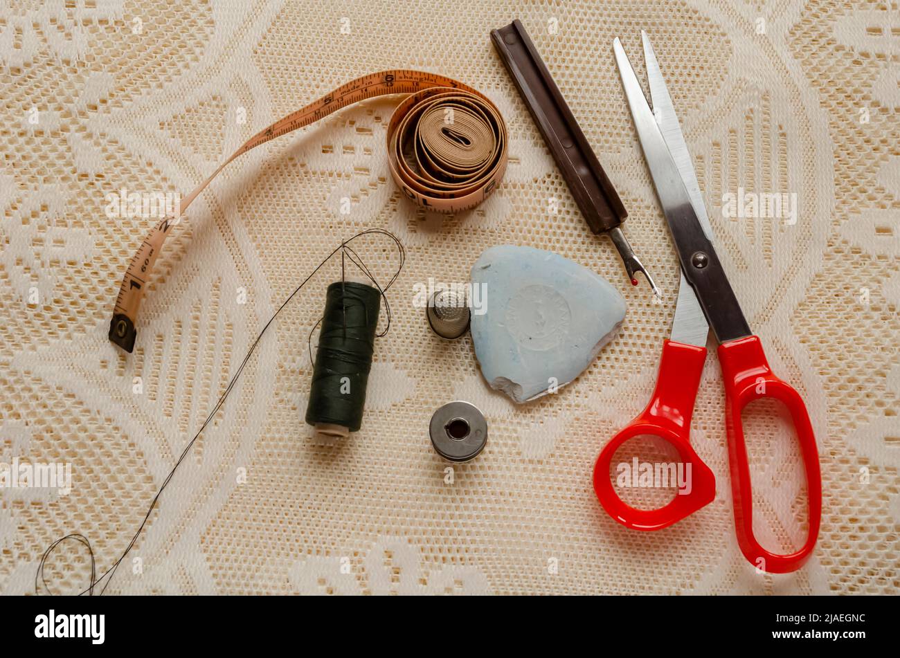 Laid out on a lacy fabric are a seam rip, tailor's chalk, needle and ...