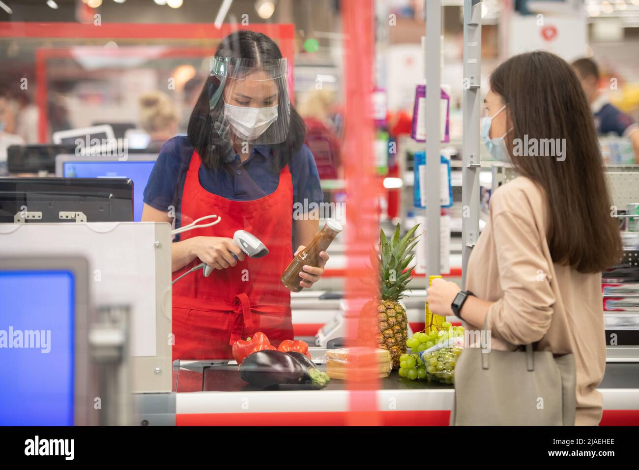 Young cashier wearing mask on face checkingout foods for customer in ...