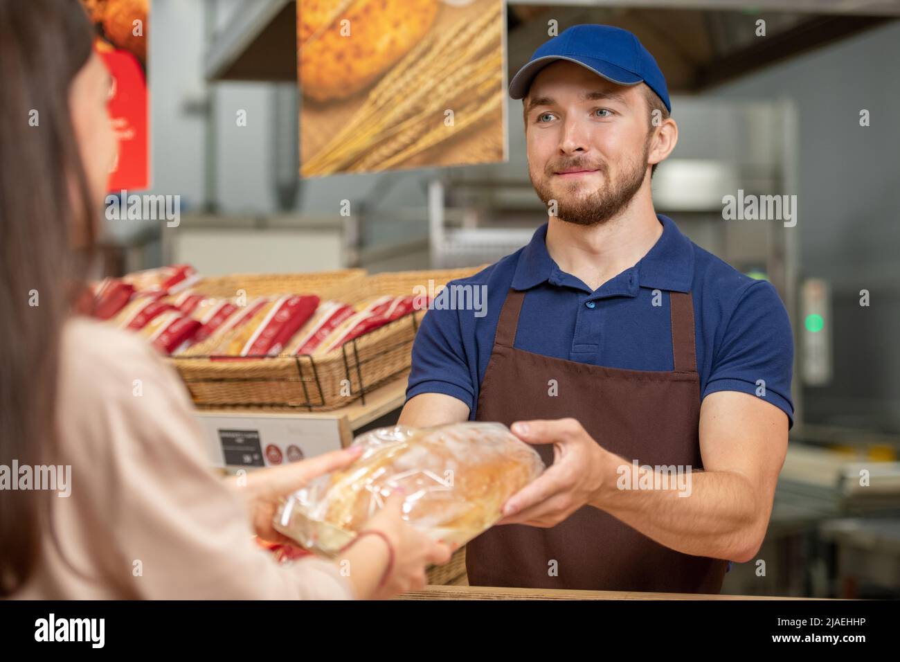Modern grocery store worker wearing uniform helping young woman to ...