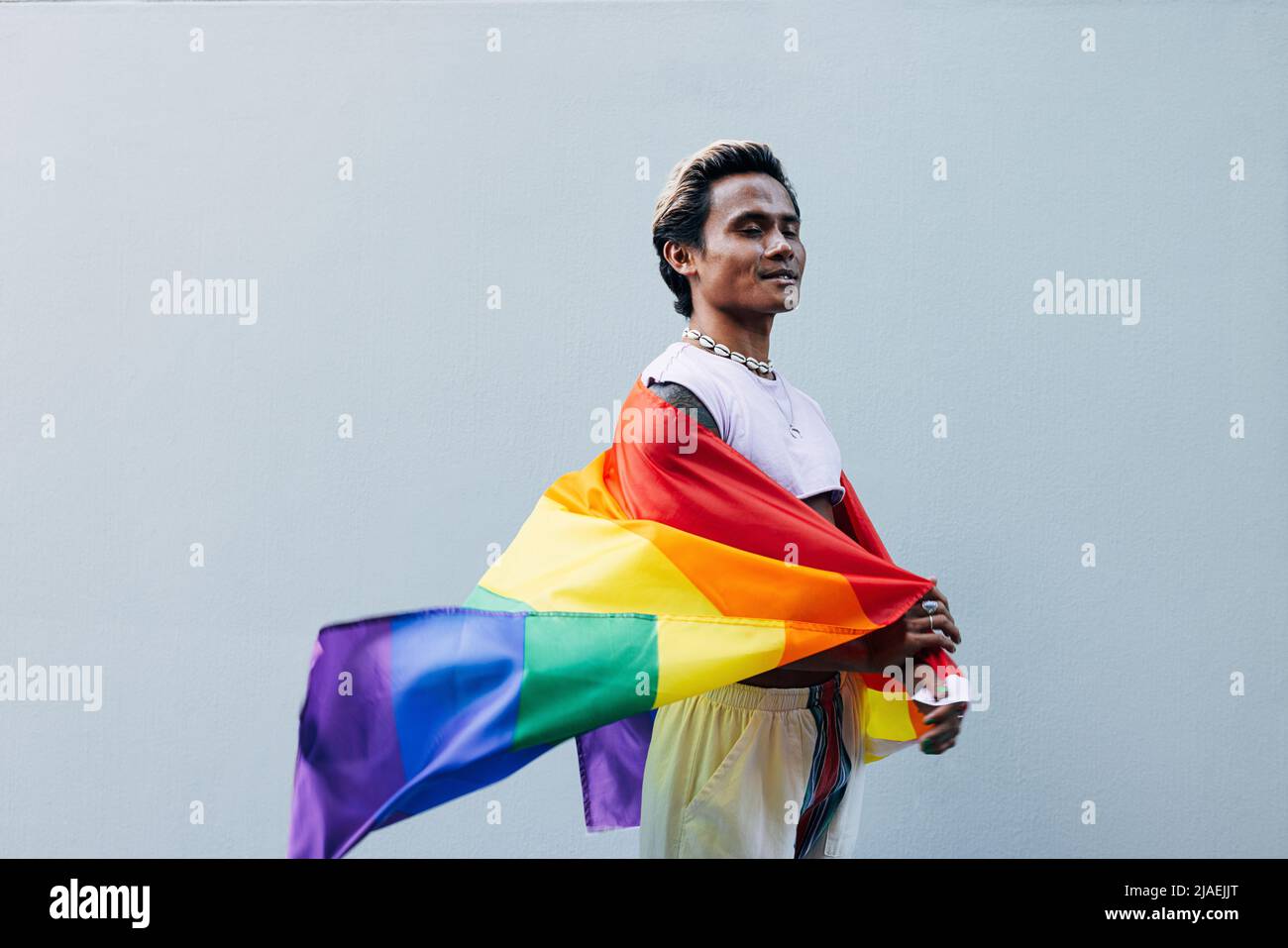 Side view of smiling male with closed eyes holding LGBT rainbow flag ...