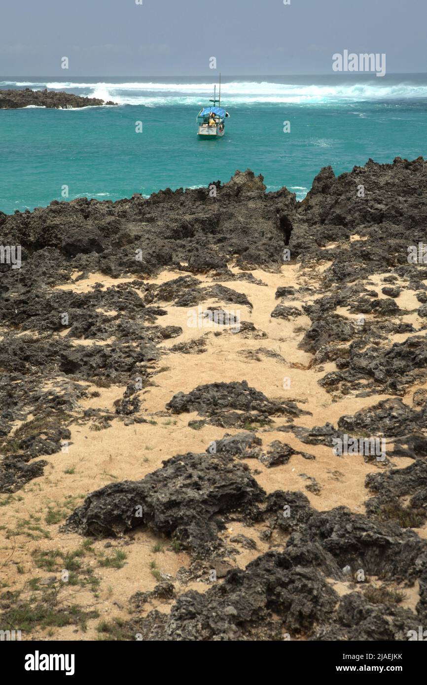 Rocky beach in a background of a fishing boat on the coastal water of ...