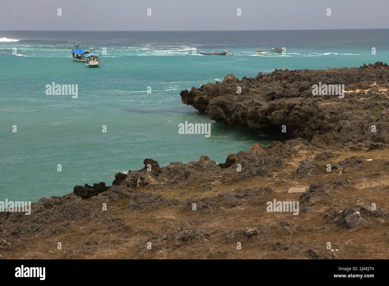 Rocky beach in a background of fishing boats on the coastal water of ...
