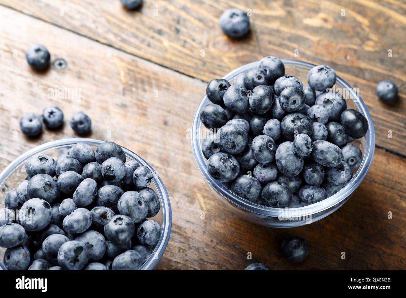 Fresh blueberries in a glass bowl and scattered on a wooden table ...