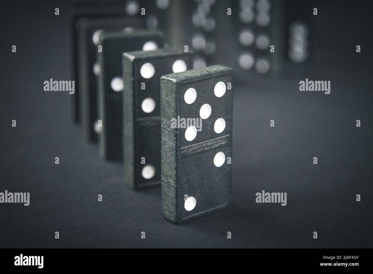 Black dominoes chain on a dark table background. Domino effect concept ...