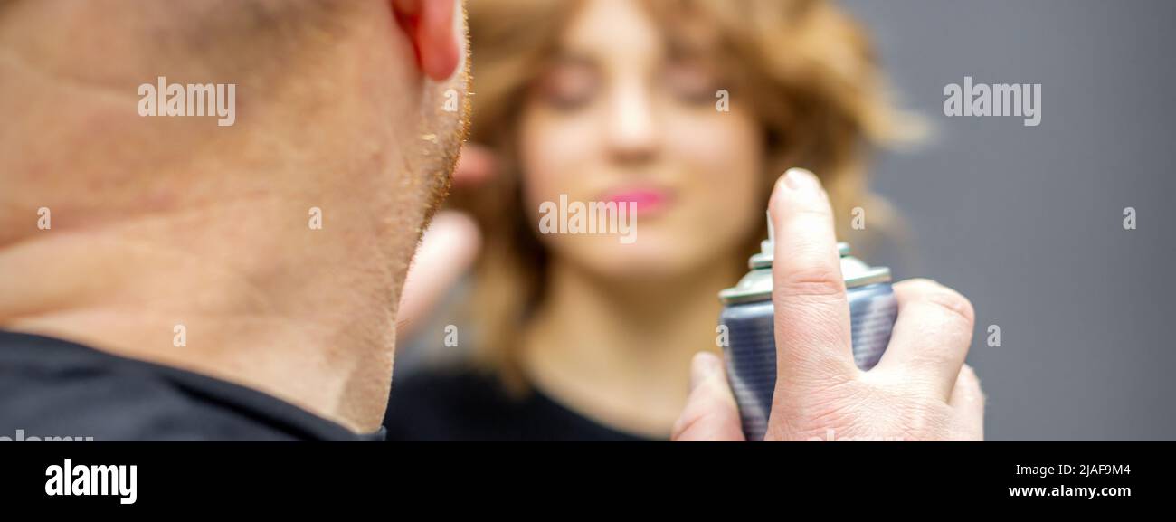 The hairdresser is using hair spray to fix the hairstyle of the young ...
