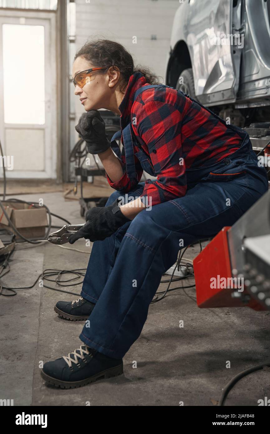 Female auto mechanic with tool sitting in car garage Stock Photo - Alamy