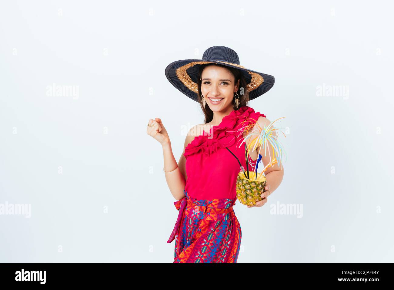 Smiling brunette girl wearing summer outfit and hat holding pineapple ...