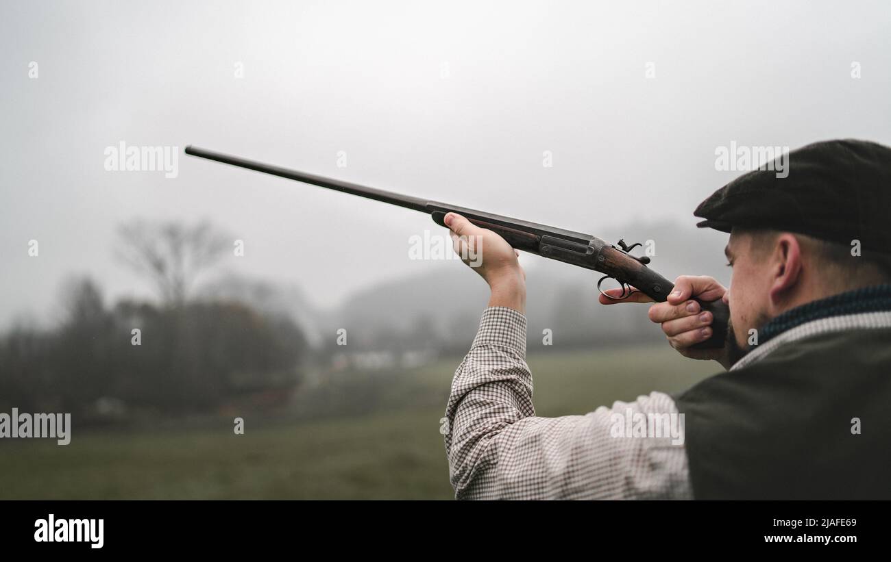 Hunter man in traditional shooting clothes on field aiming with shotgun ...
