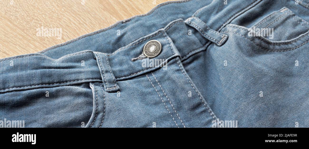 Close up detail of pocket and button front view of light blue jeans ...