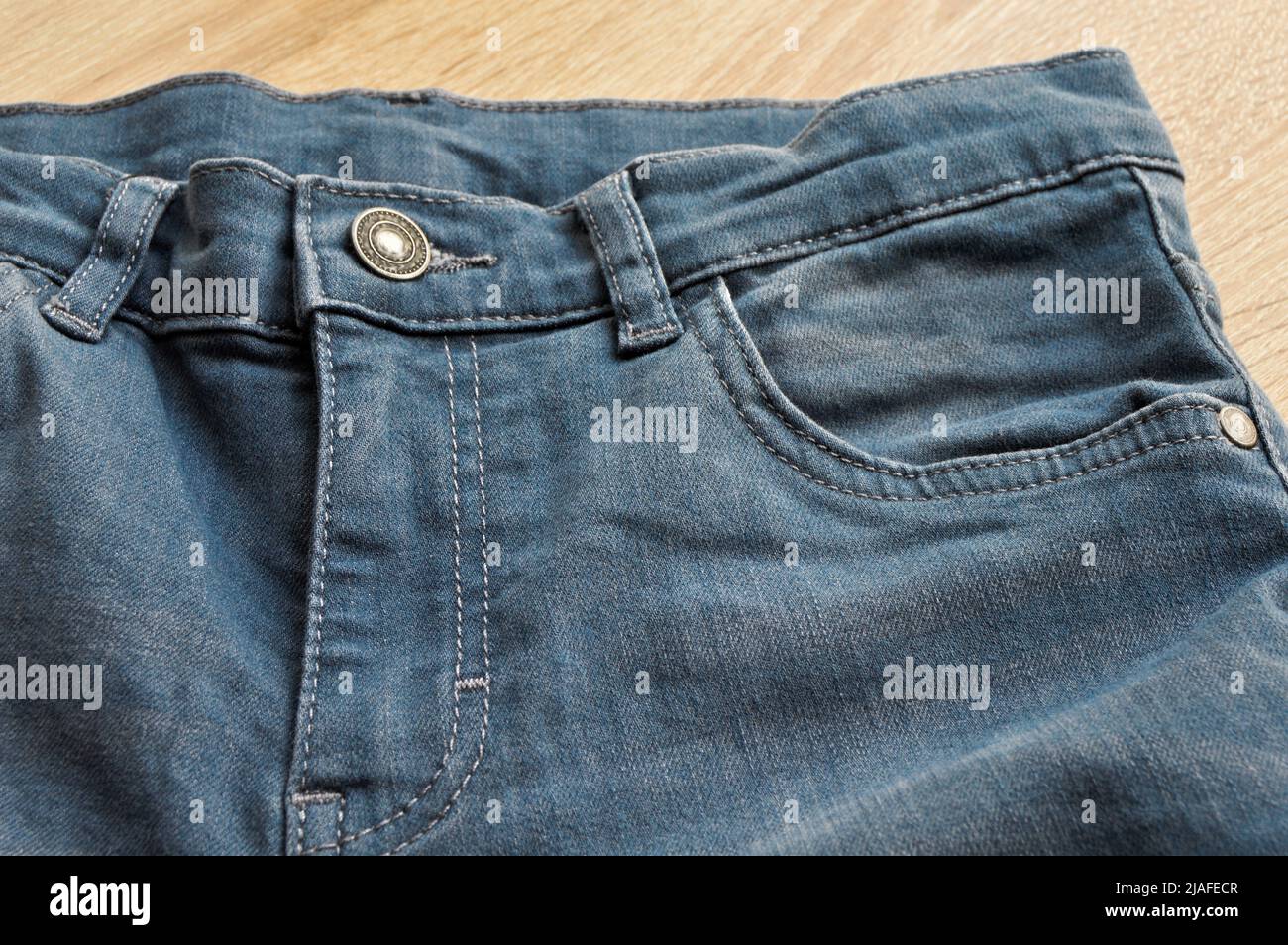 Close up detail of pocket and button front view of light blue jeans ...
