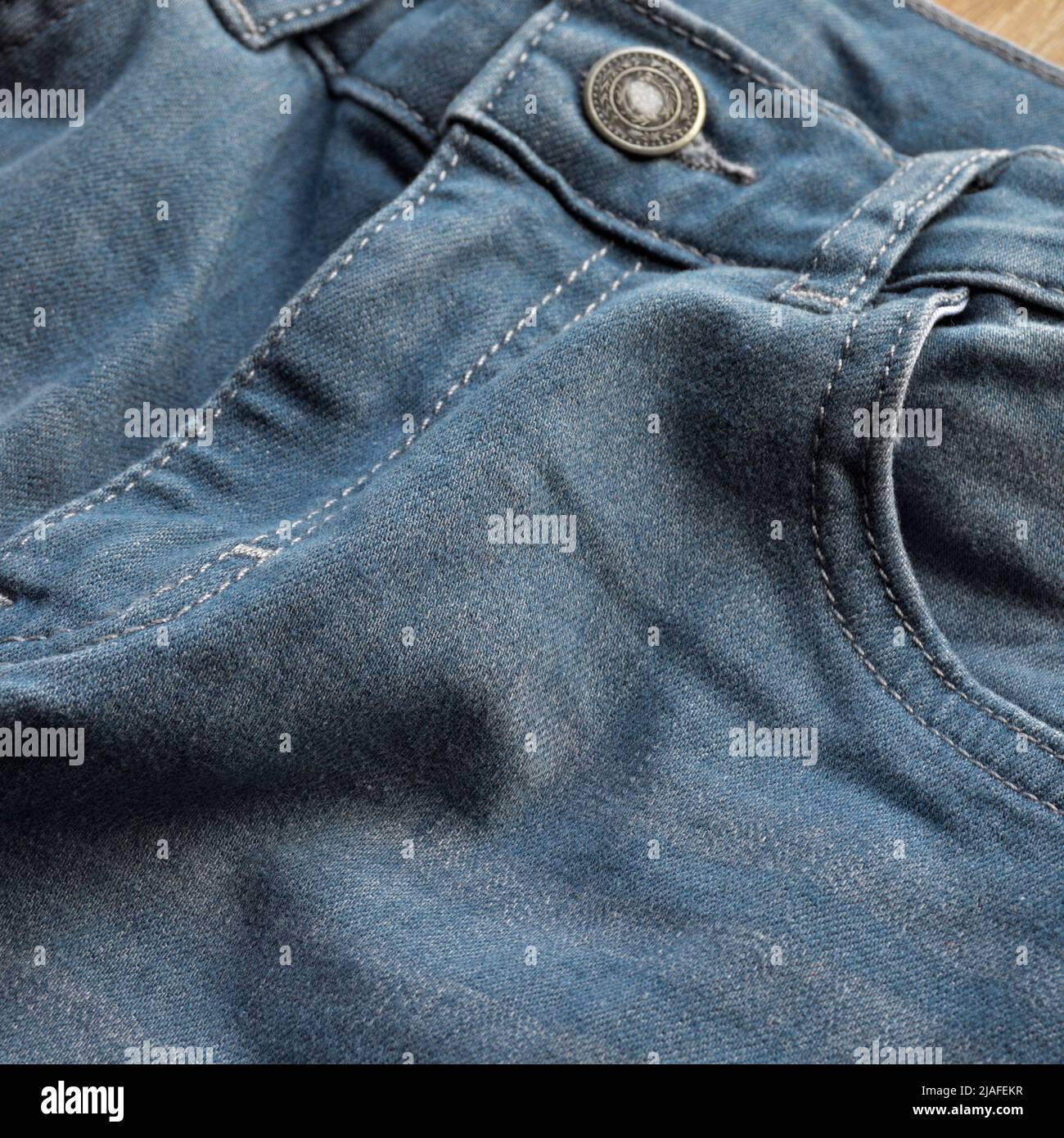 Close up detail of pocket and button front view of light blue jeans ...