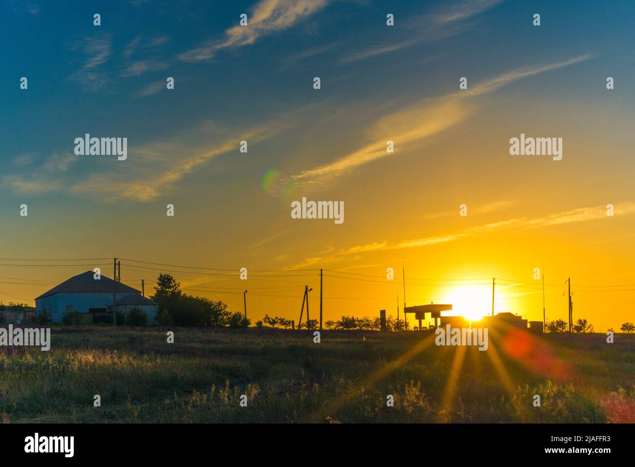 Rural sunset landscape. Sun with rays over the track with wires and ...
