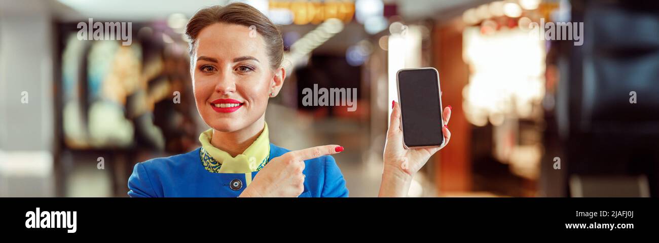 Joyful woman flight attendant pointing at smartphone at airport Stock ...