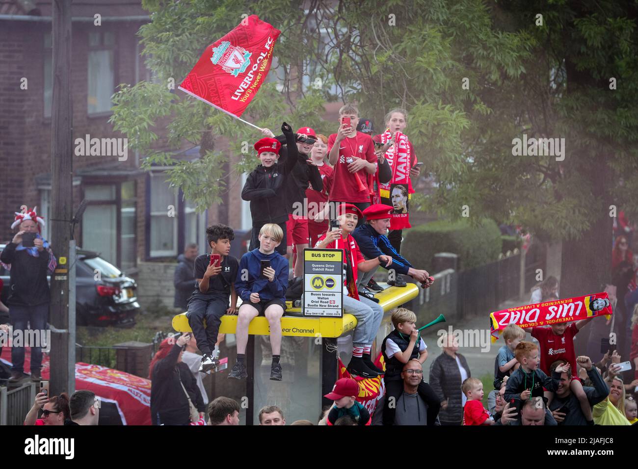 Young supporters stand on top of a bus shelter and cheer on the ...