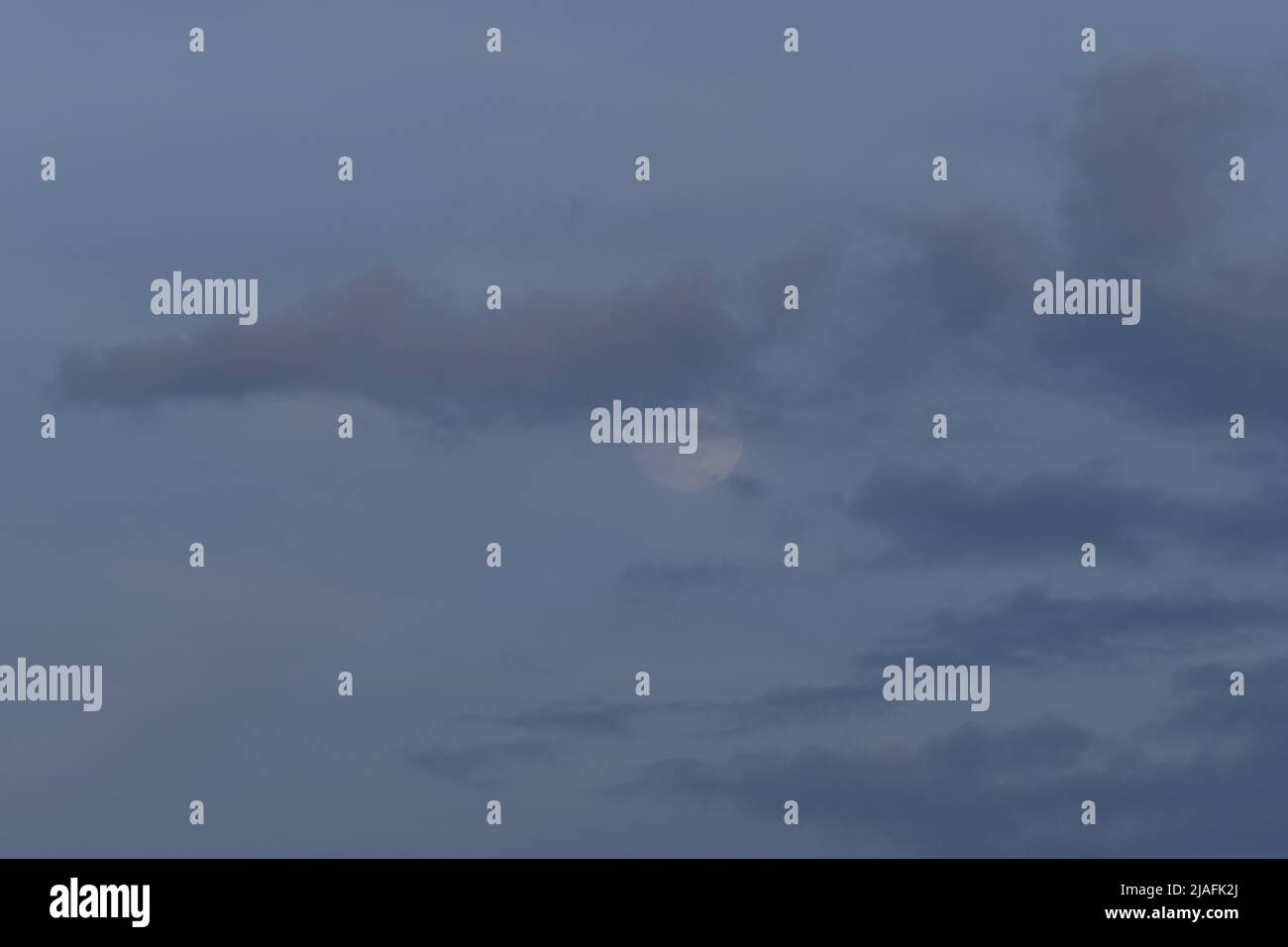 Full moon rises behind clouds at dusk, lunar phase of natural satellite ...