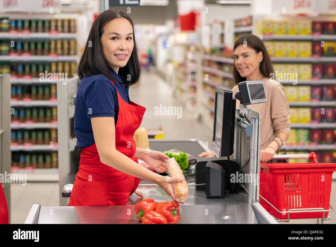 Vertical portrait of attractive Asian cashier wearing red apron working ...
