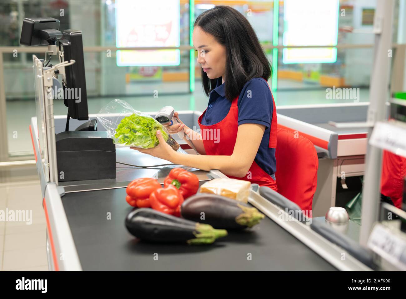 attractive Asian cashier wearing red apron selling fresh vegetables to ...
