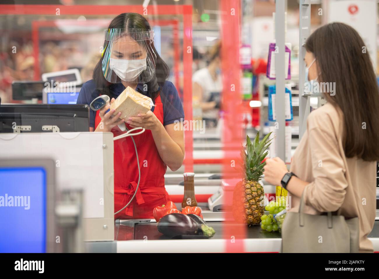 Young cashier wearing mask on face checkingout foods for customer in ...