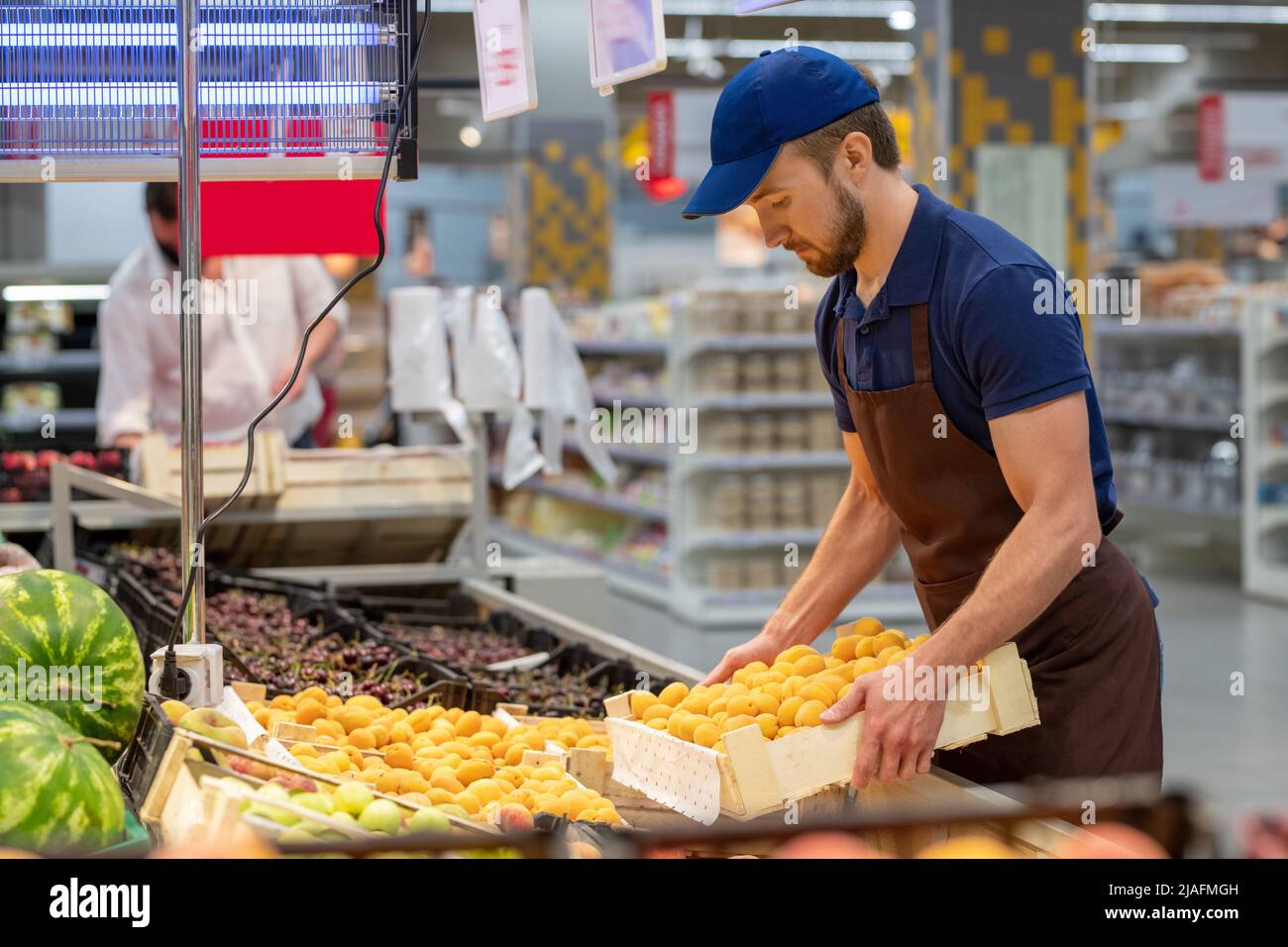 Side view shot of man wearing apron working in store setting out fresh ...