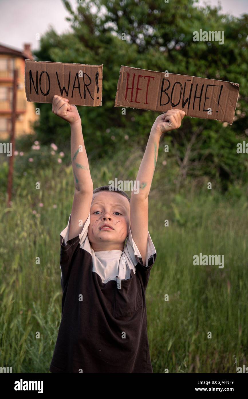 A boy with a grimy face and sad eyes holds a cardboard poster with the ...