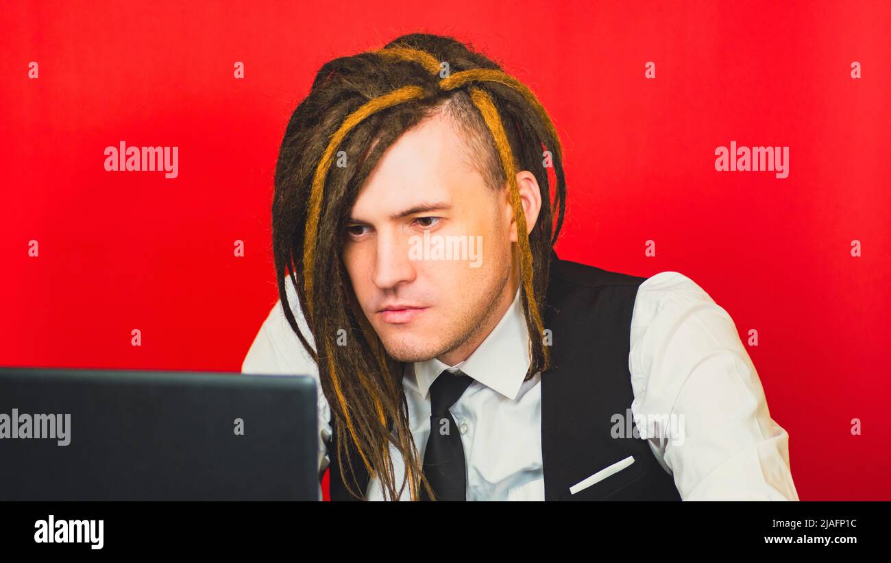 Young conceptual man in business suit working at laptop red background ...