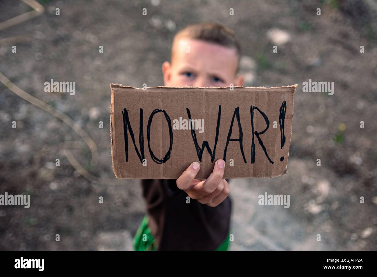 A boy with a grimy face and sad eyes holds a cardboard poster with the ...